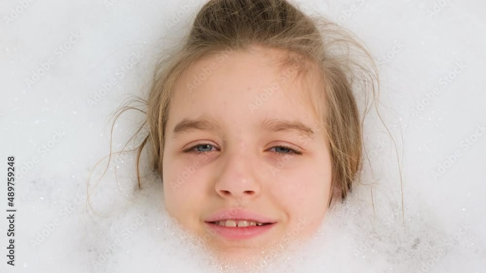 Portrait of cheerful teen girl lying in bath with thick soap foam and ...