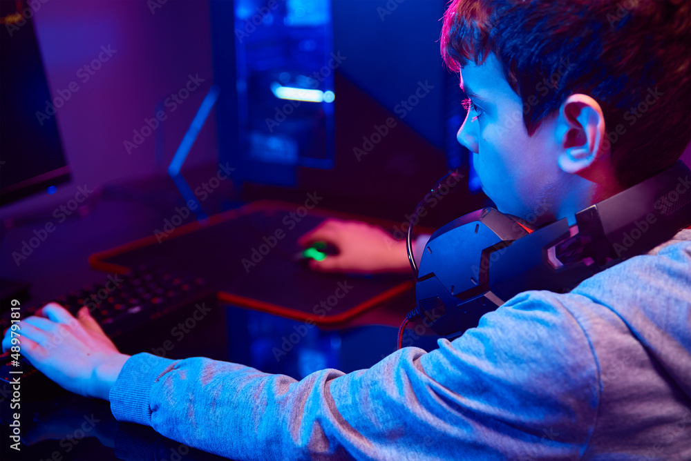Teenager boy play computer video game in dark room, use neon colored ...