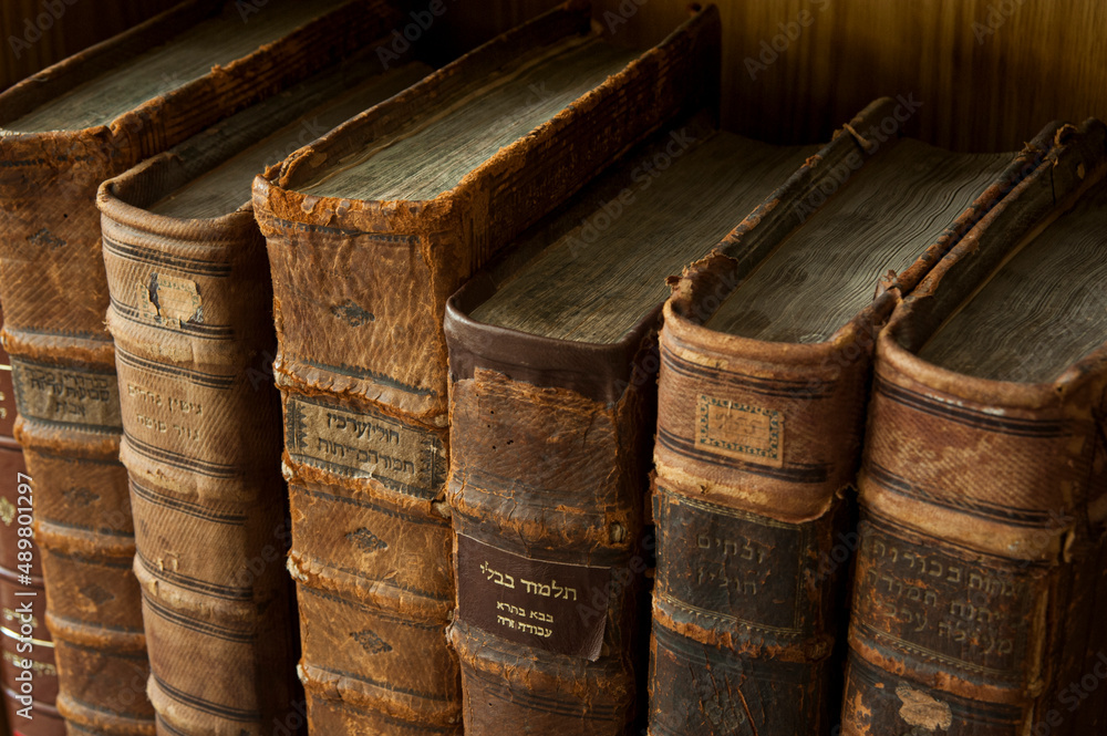 Dusty, worn and faded leather-bound Jewish holy books stacked upright ...