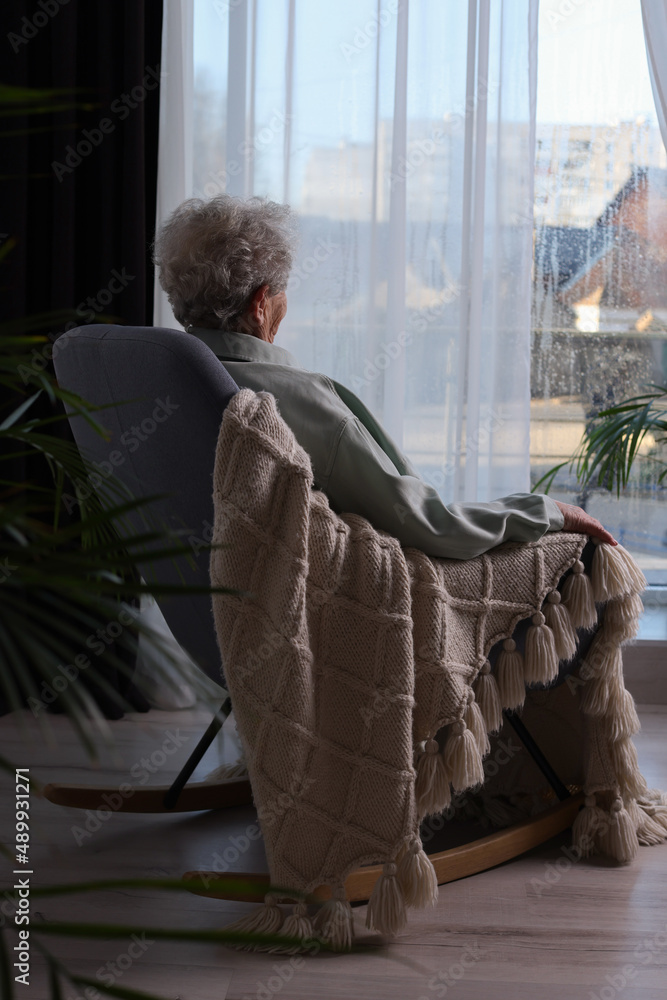 Elderly woman sitting in rocking chair indoors, back view. Loneliness ...