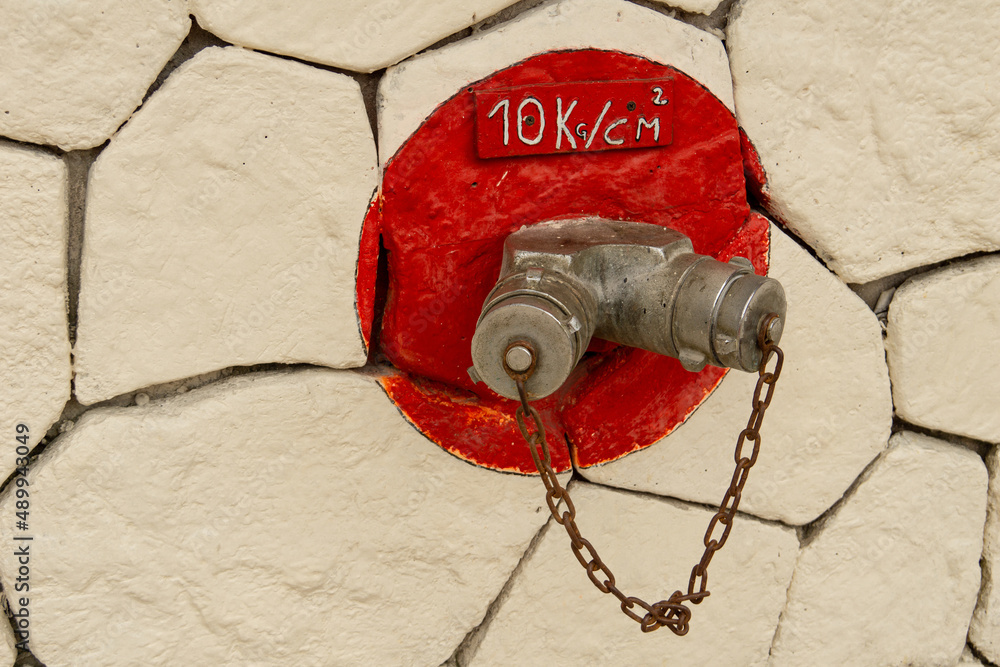 Fire hydrant with a chain on a red background. On the stone wall, the ...