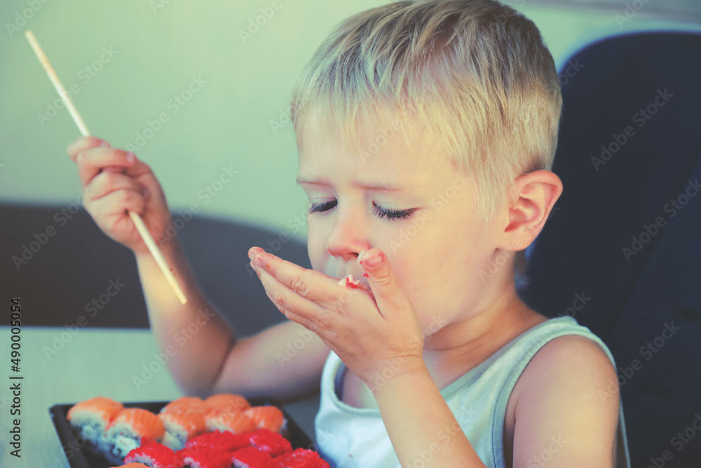 The child is eating sushi. Boy learning to eat rolls with chopsticks ...