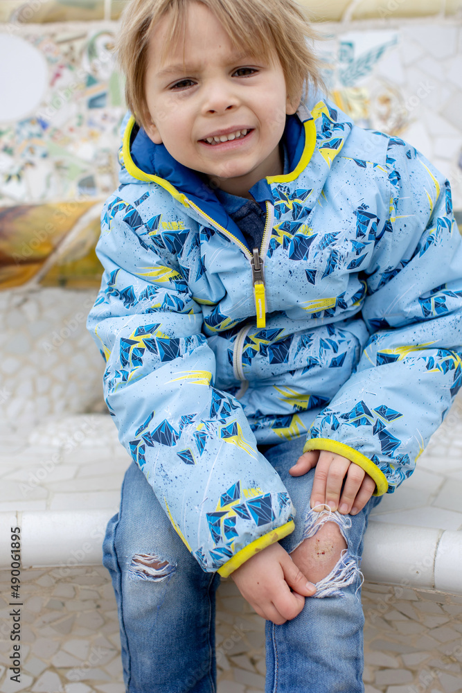 Little boy, showing wounded knee from a fall, sitting on a bench Stock ...