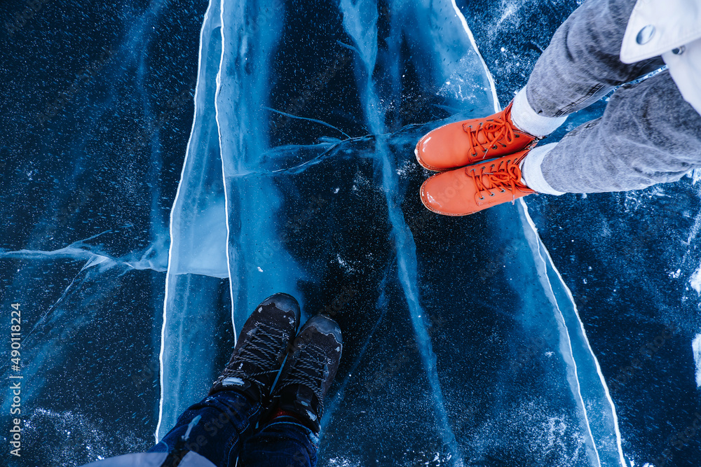 Fragile thin brittle ice underfoot. Male and female feet on ice. Cracks ...