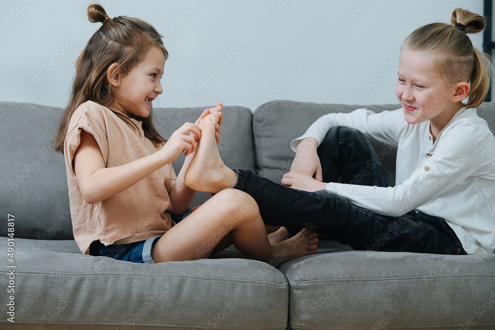 Mischievous girl trying to tickle boy's foot, they both laugh. Stock Photo | Adobe Stock