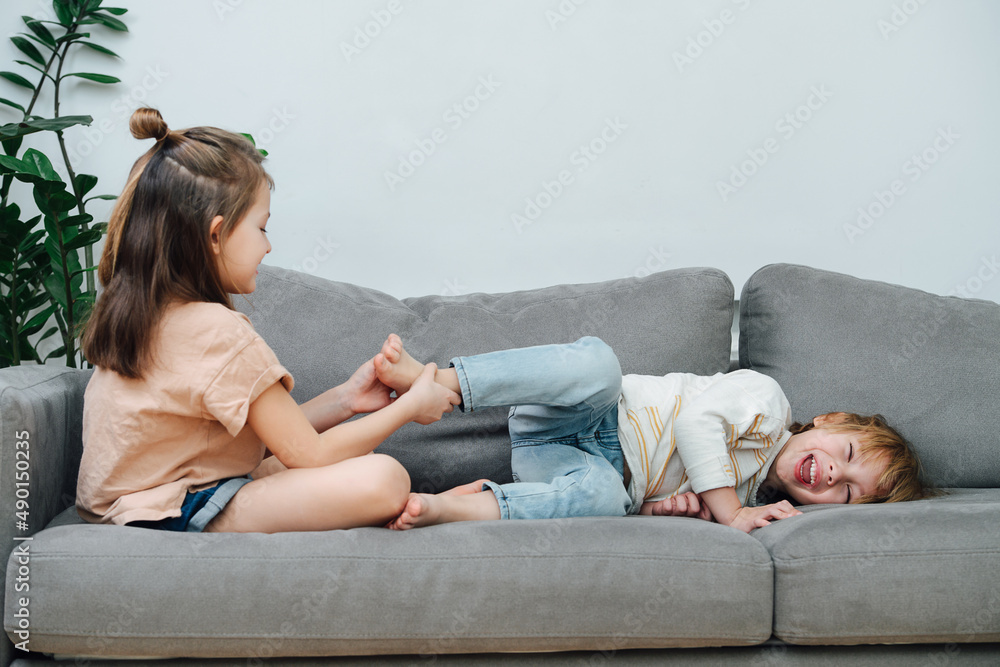 Dominant little girl tickling to tickle boy's foot, making him roll and laugh Stock Photo ...