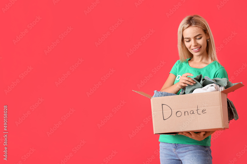 Beautiful woman holding box with donation clothes on red background ...