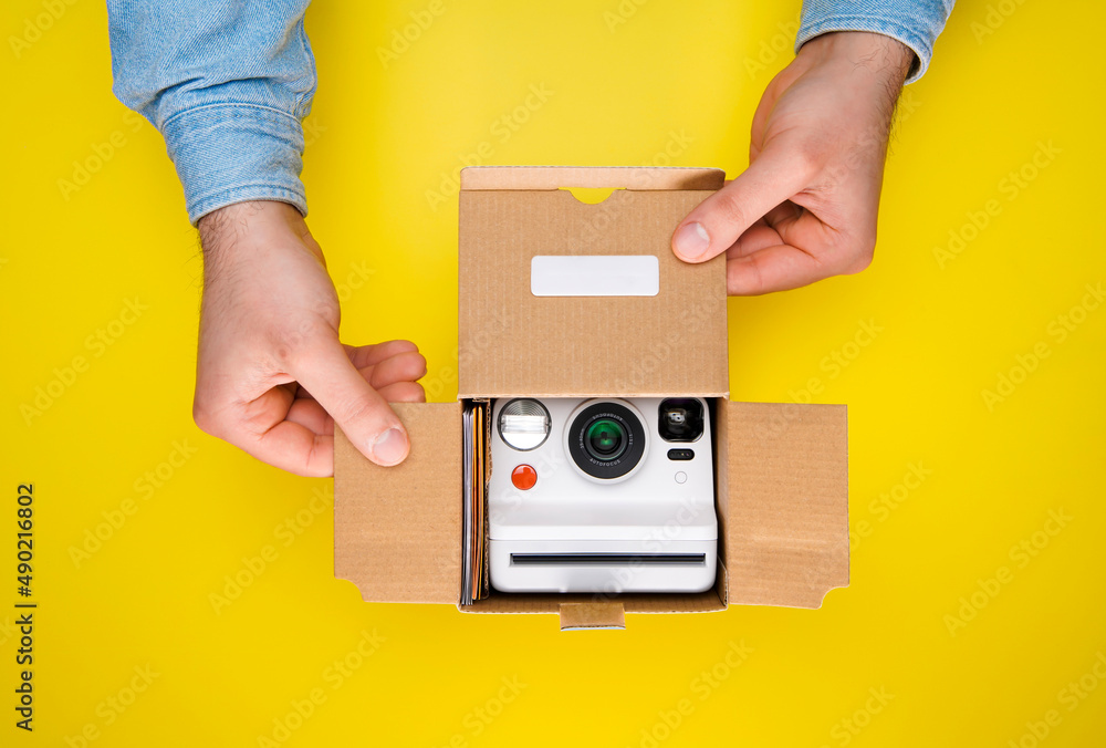 Top down unboxing of a product package on a yellow background. Hands ...