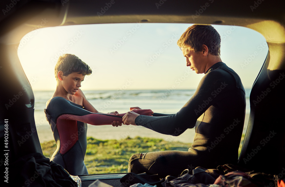 Thats what big brothers are for. Shot of a young surfer helping his ...