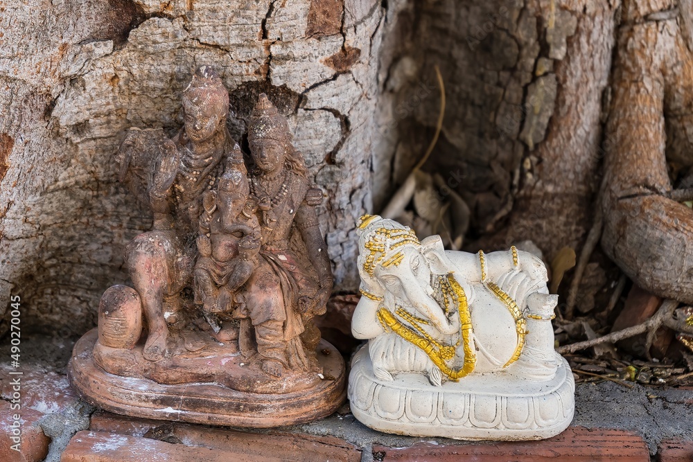 old clay broken statue of the hindu god are laid under a tree in a Thai ...