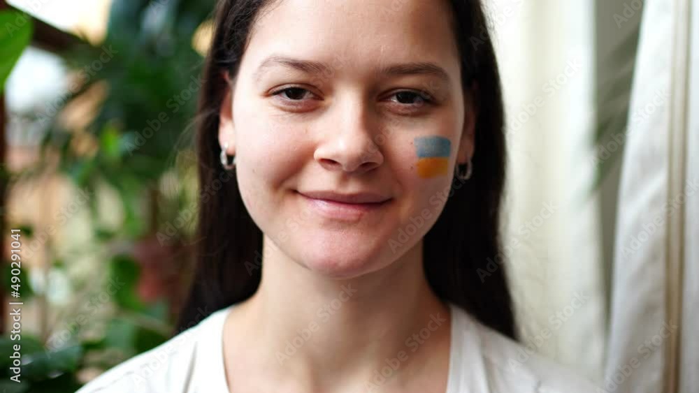 A smiling young Ukrainian girl with the flag of Ukraine on her face is ...