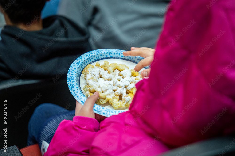 Young girl's hands eating a funnel cake with powdered sugar on paper ...