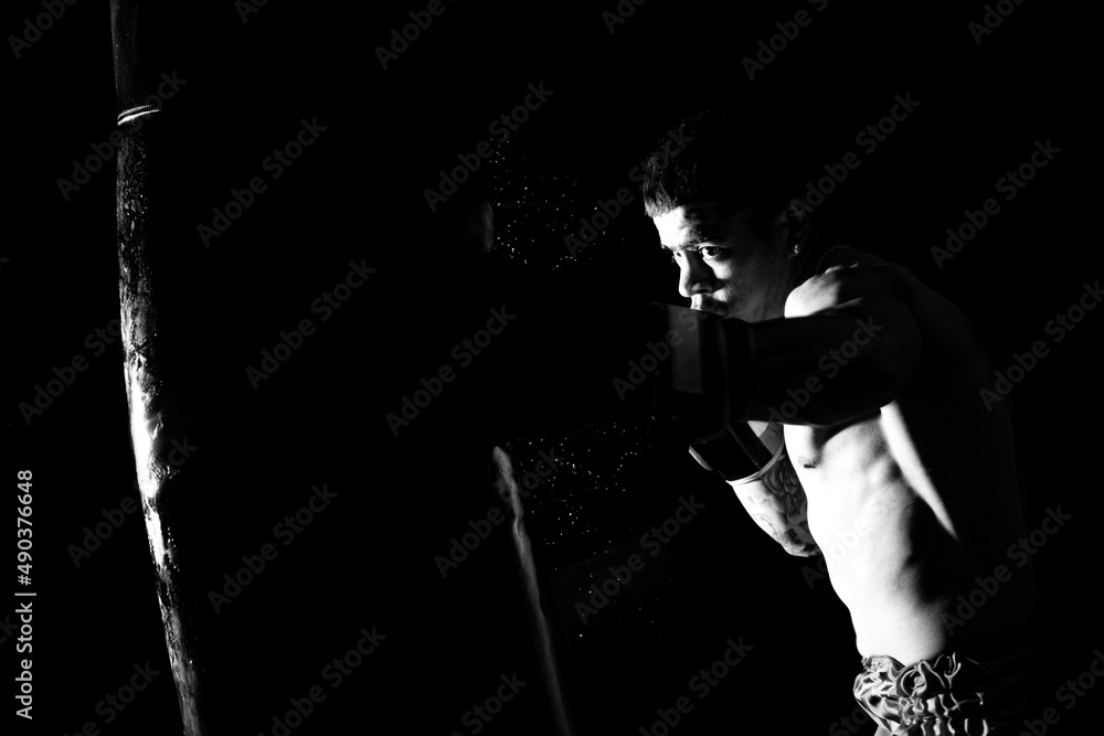 Young man hits a punching bag over black background. Black and white ...