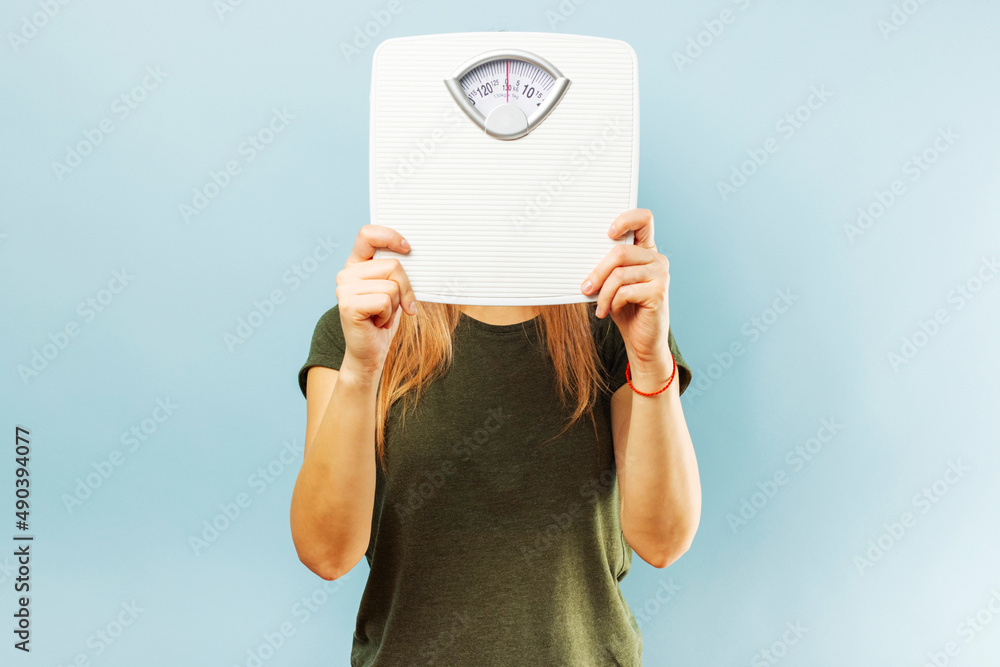 Woman with weight scale. Young slim woman hiding her face behind weight ...