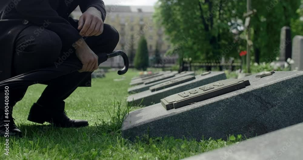 Sad young man in suit stands on the grave of the city cemetery. Funeral ...