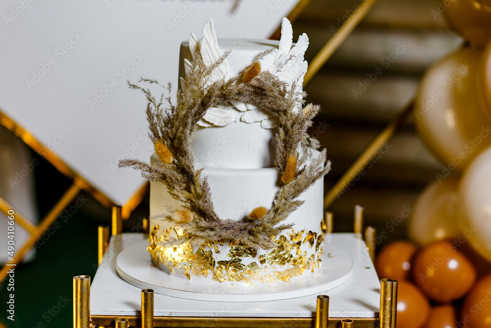 Sweet gold coloured christening cake with angel wings and natural ornaments in restaurant after ...
