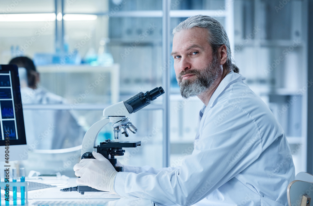 Portrait of mature bearded scientist looking at camera while working ...