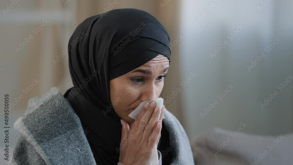 Close up sick upset young girl in hijab sneeze wipe nose with paper ...