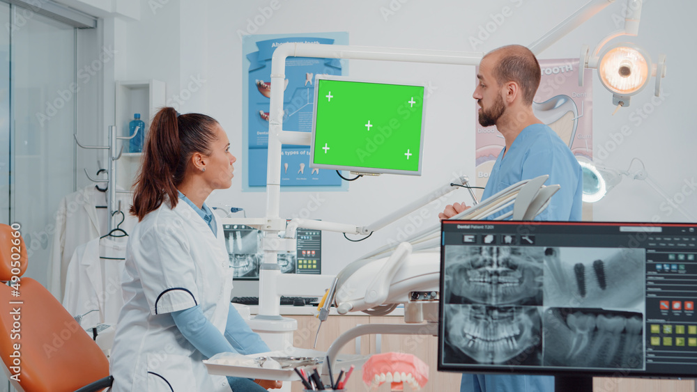 Dentist and assistant looking at green screen on monitor in dental ...