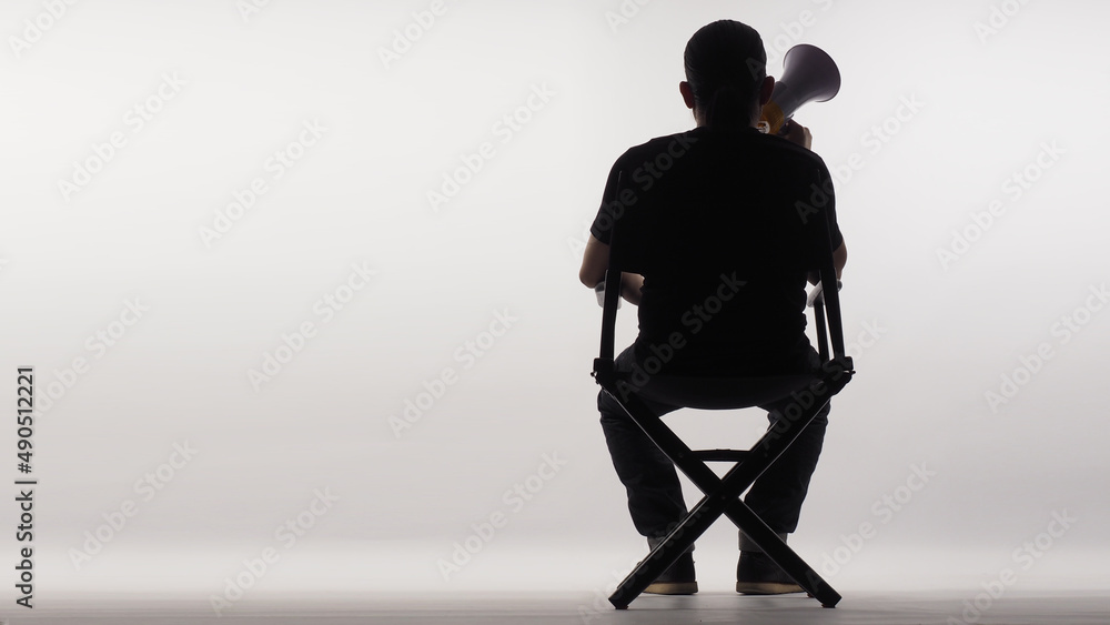 Back of Asian man sitting on black director chair. He is holding a ...