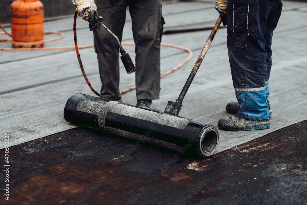 Professional workers insulating rooftop with bitumen membrane and ...