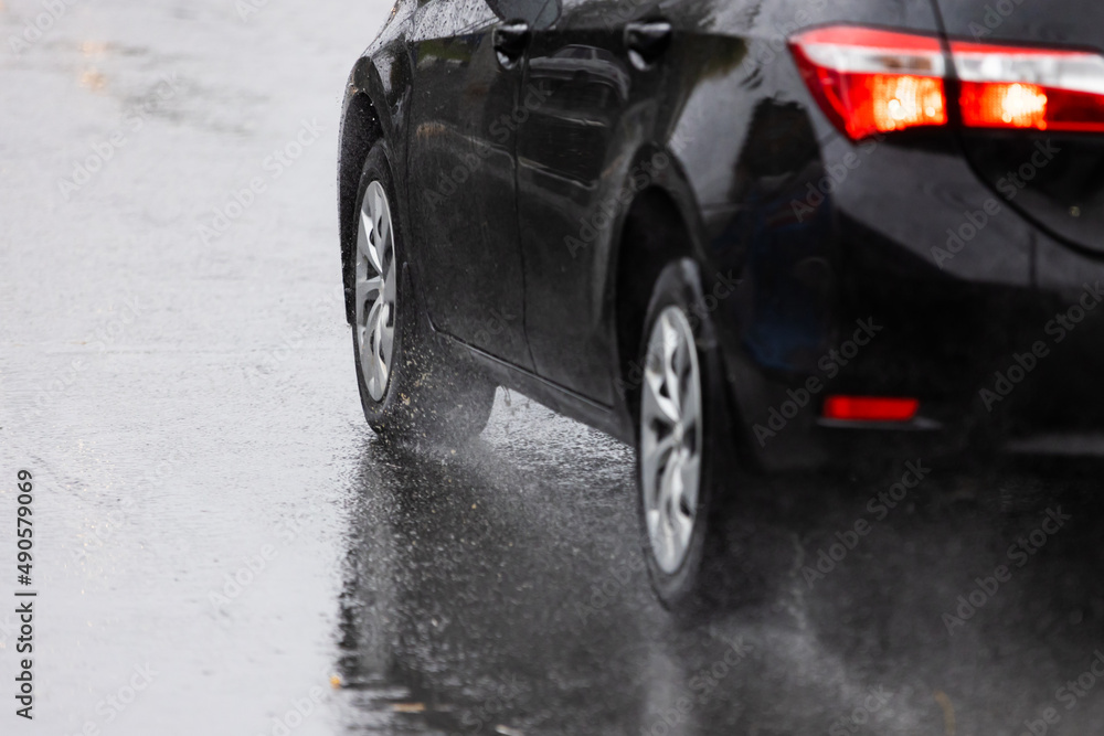 rain water splash flow from wheels of black car moving fast in daylight ...