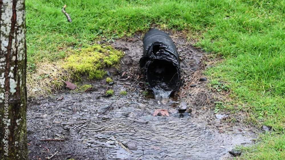 Excess rainwater flowing out of round black storm water management pipe ...