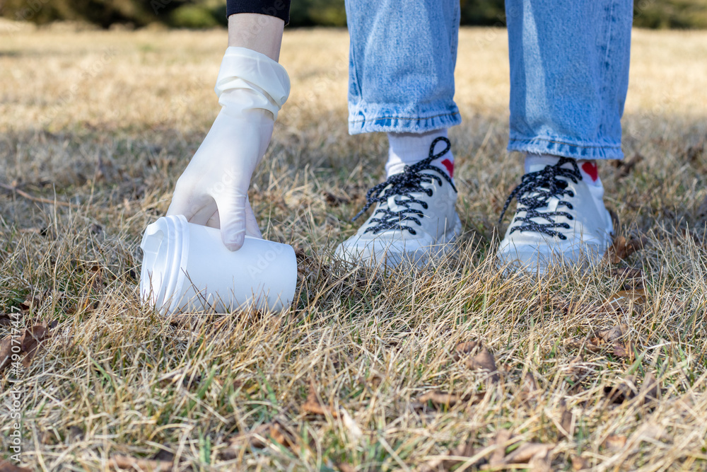 young girl, volunteer is picking garbage from the dry grass, in a ...