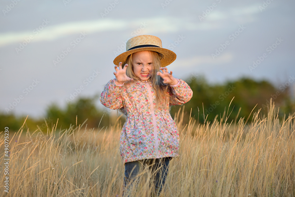 A preschool girl with golden hair and a straw hat shows anger and ...