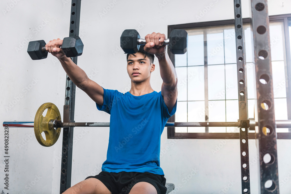 A young asian man wearing a blue shirt and seated on a bench does ...