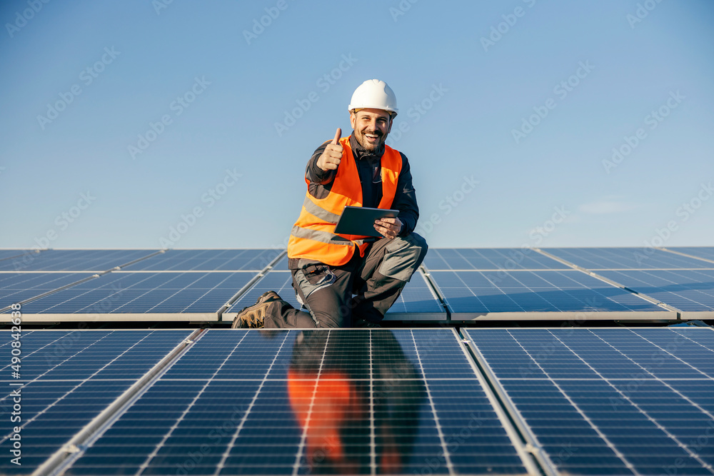 A handyman on roof surrounded by solar panels giving thumbs up for eco ...