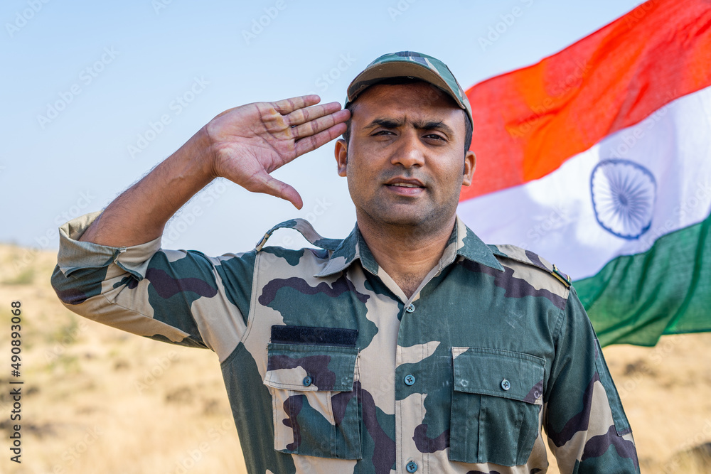 army officer saluting by looking at camera in front of waving Indian ...