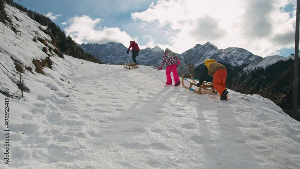 Two kids with sleds climbing to the top of the slope with their father ...