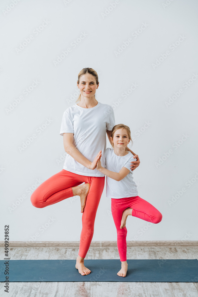 A happy mother and daughter stand in Tree pose. Vrishasana.girls smile ...