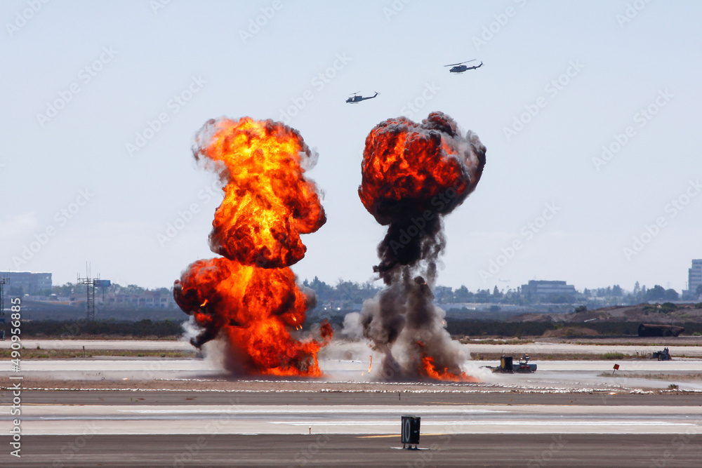 Bomb explosion at an airfield with combat helicopters in the background ...