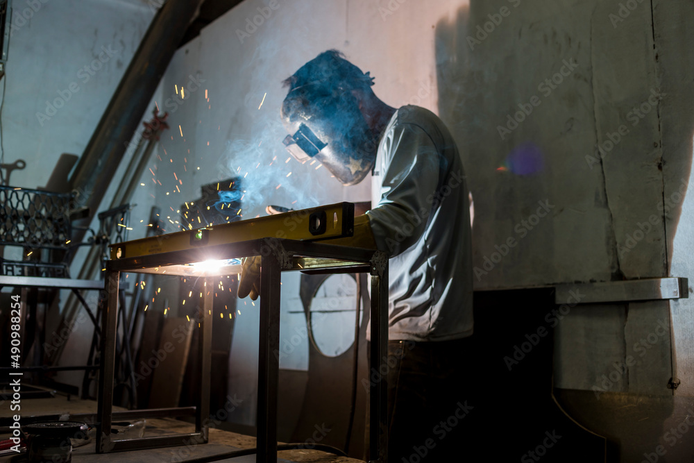 Welding the corner joint of a steel bench. Using a level bar to check ...