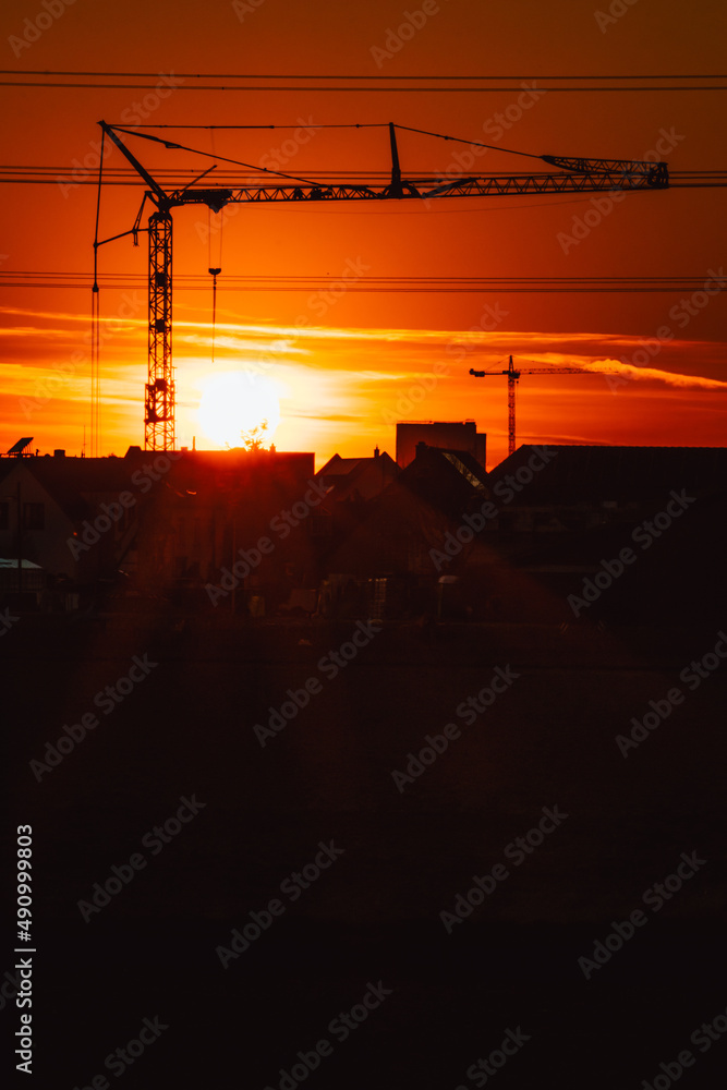 Tall construction crane silhouette in orange sky sunset shows ...