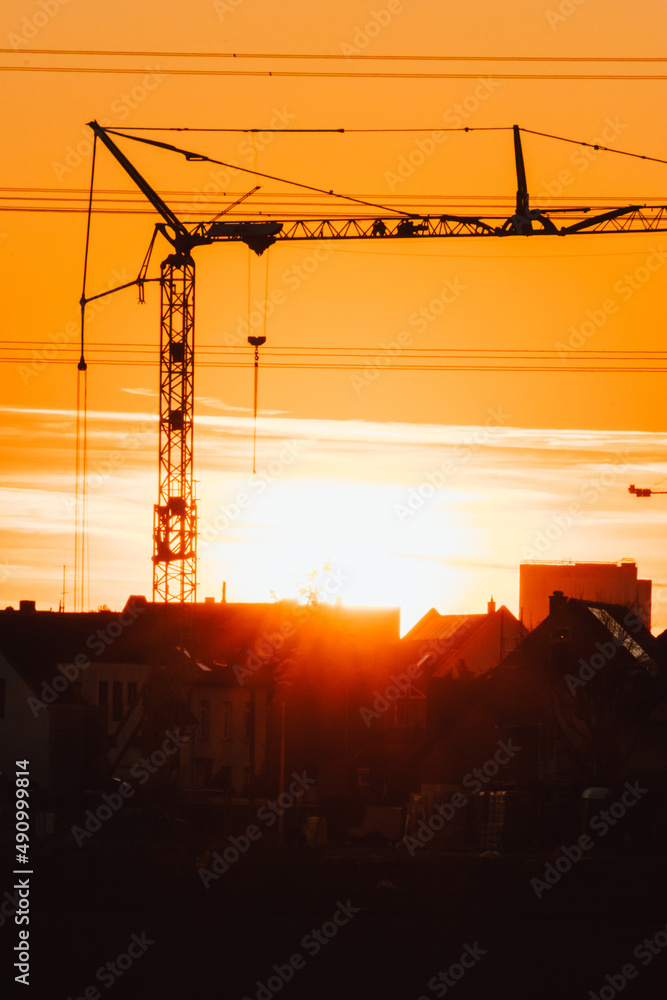 Tall construction crane silhouette in orange sky sunset shows ...