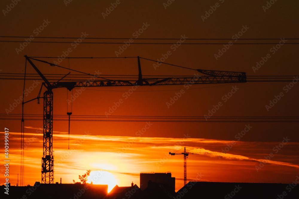 Tall construction crane silhouette in orange sky sunset shows ...