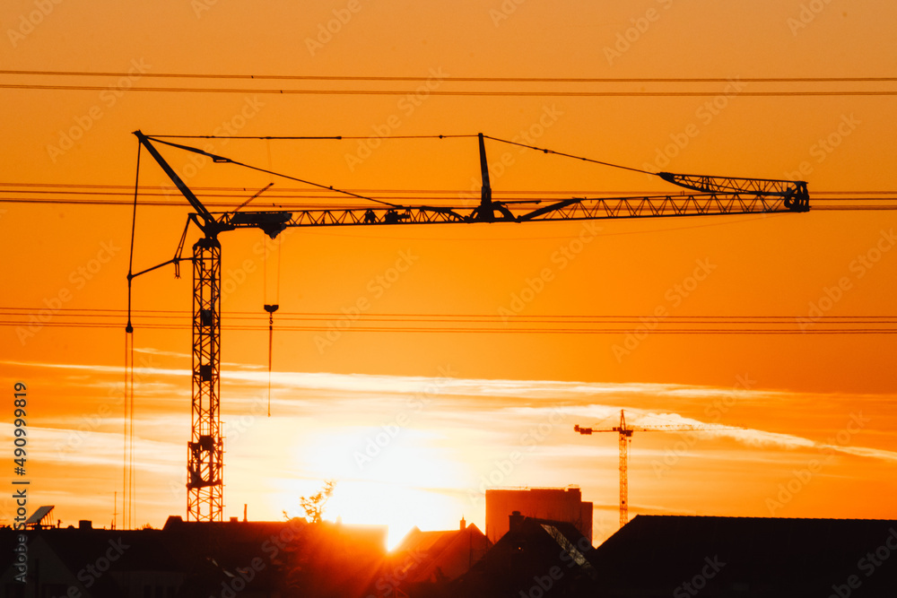 Tall construction crane silhouette in orange sky sunset shows ...