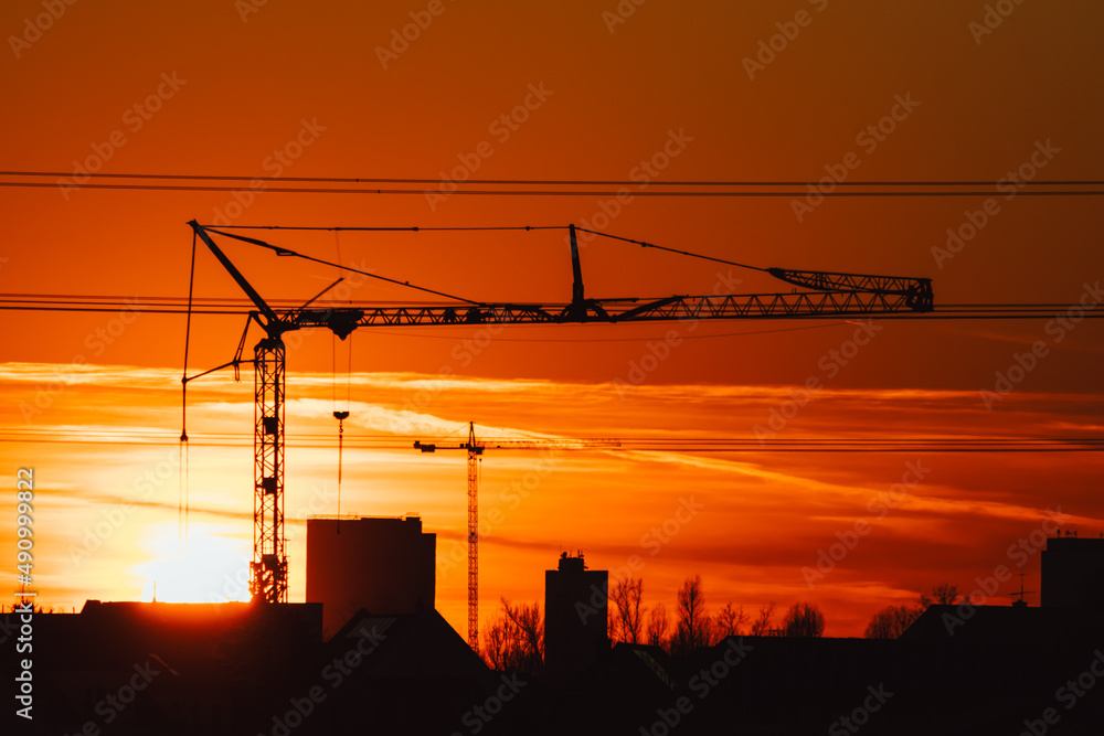 Tall construction crane silhouette in orange sky sunset shows ...