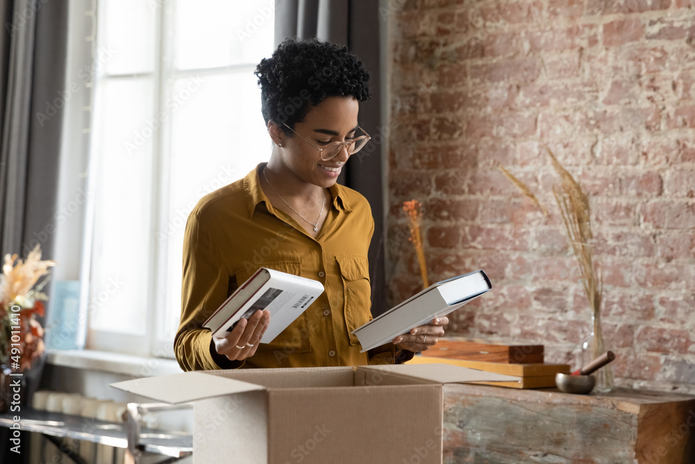 Positive happy African student girl unpacking box with books, receiving ...