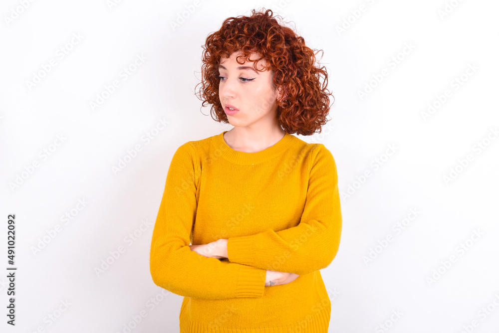 Displeased young redhead girl wearing yellow sweater over white ...