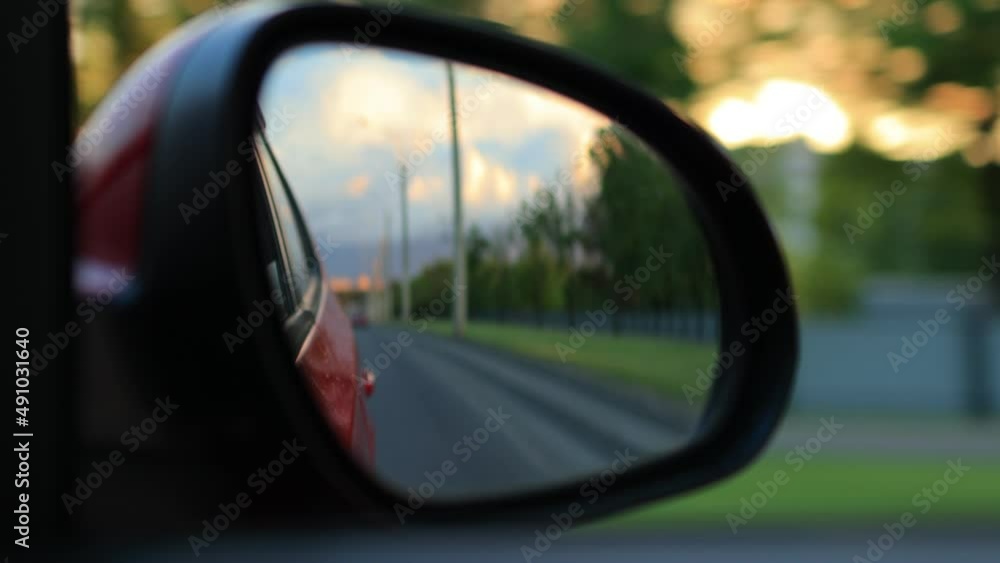 View in the side rear view mirror of a car driving a red car on a ...