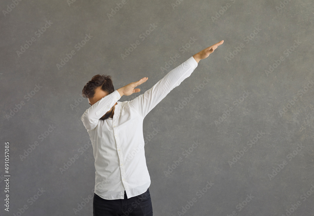 Happy young guy doing a dab dance arm move standing on a grey studio ...