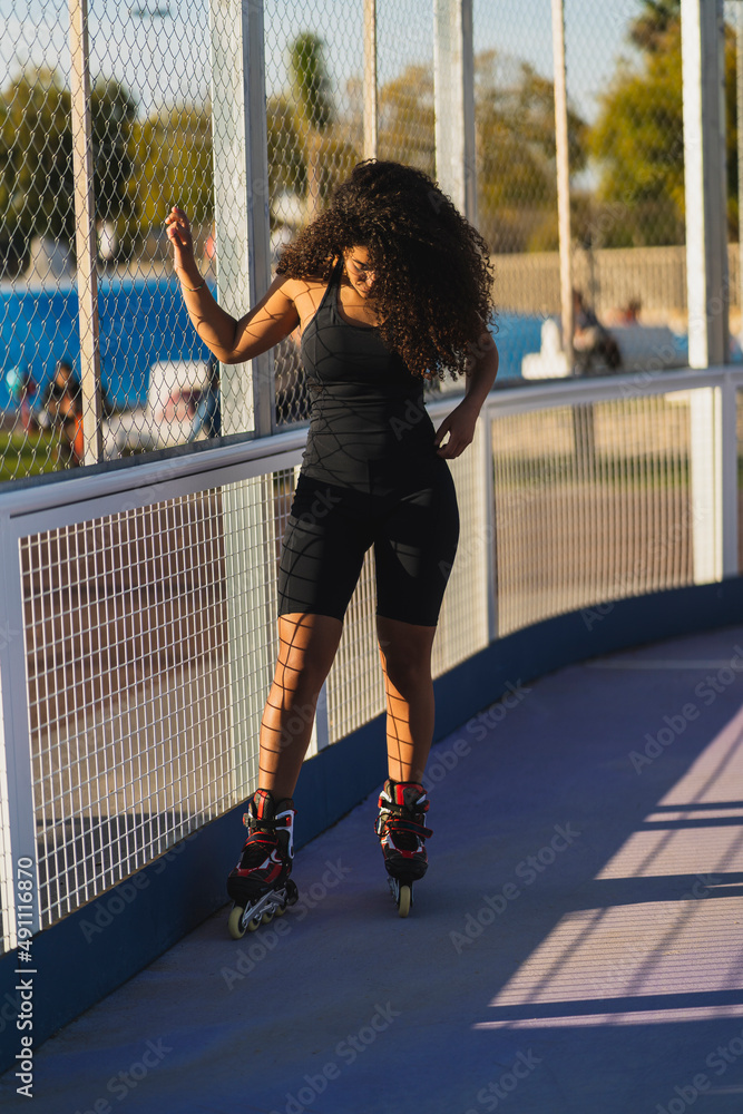 Chica morena con pelo rizado en ropa deportiva patinando en pista azul ...