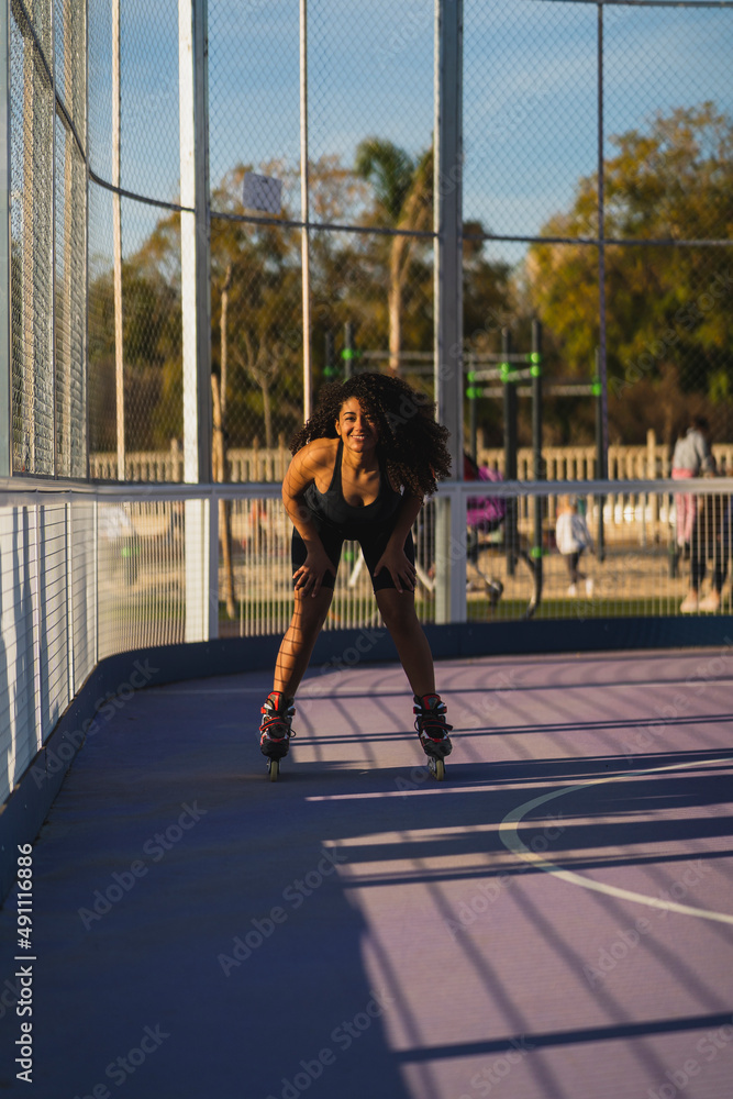 Chica morena con pelo rizado en ropa deportiva patinando en pista azul ...