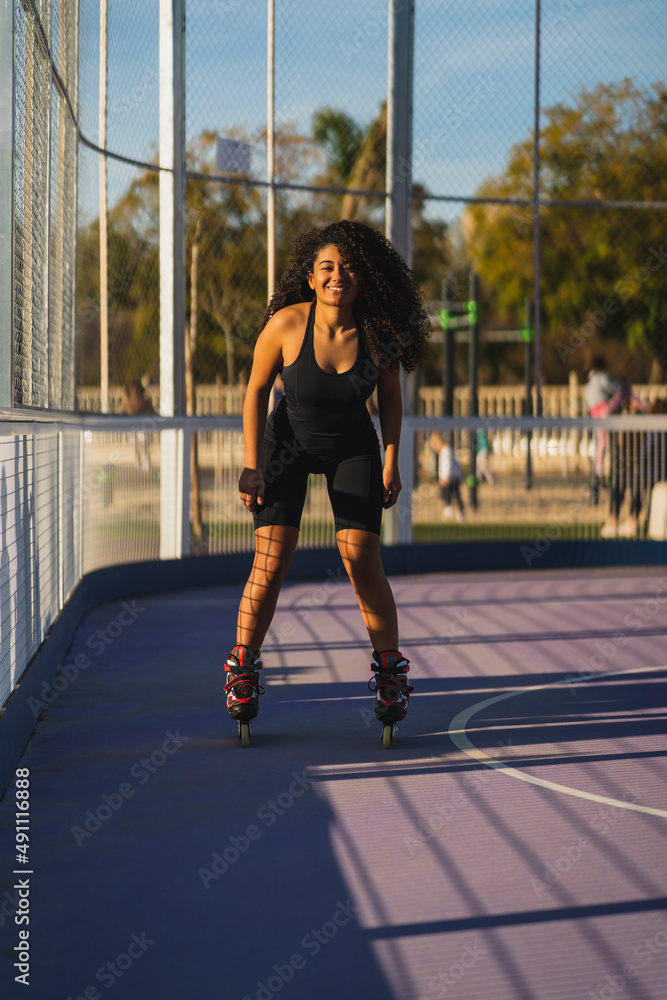 Chica morena con pelo rizado en ropa deportiva patinando en pista azul ...