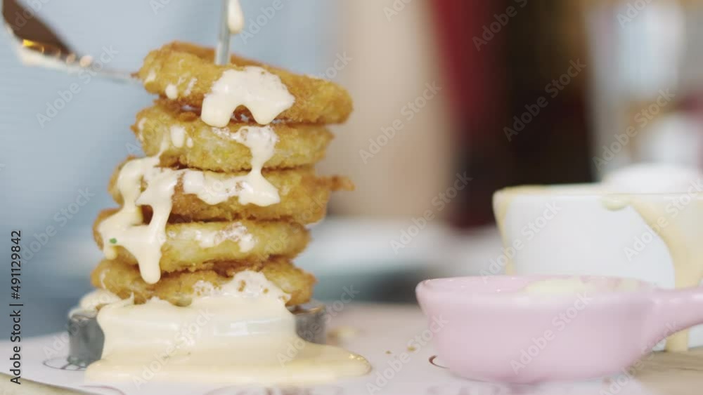 close up and slow motion of pouring cheese sauce in stack of onion ...
