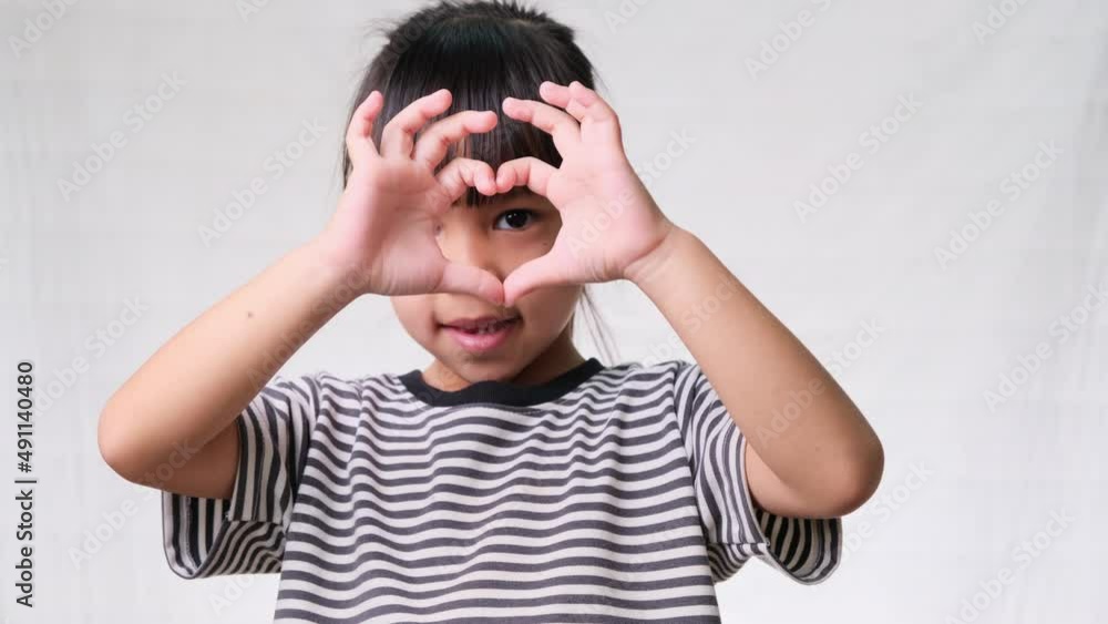 Cute little girl doing heart-shaped hands on eyes over a white studio ...